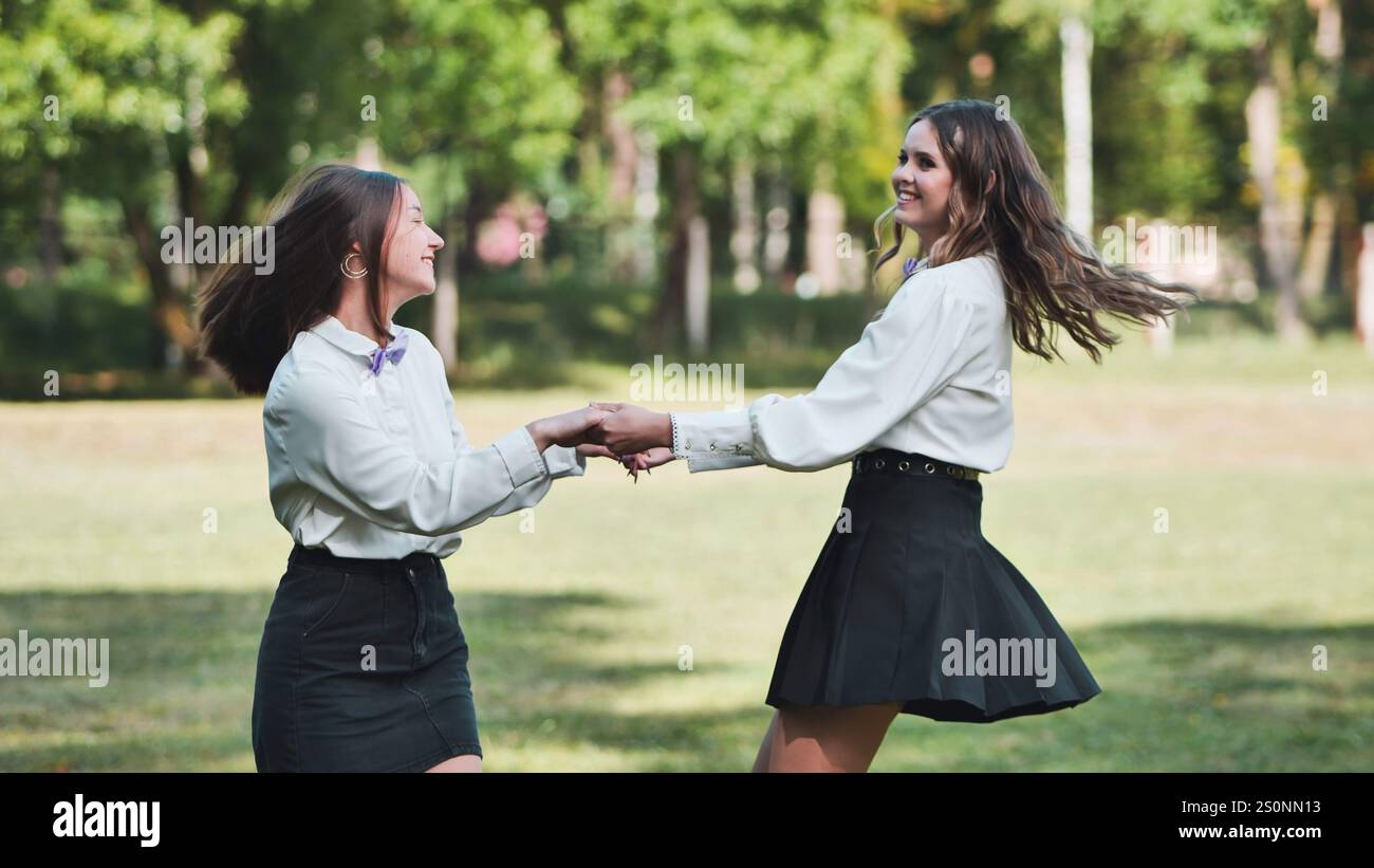 Two delighted schoolgirls twirling and holding hands in the park on ...