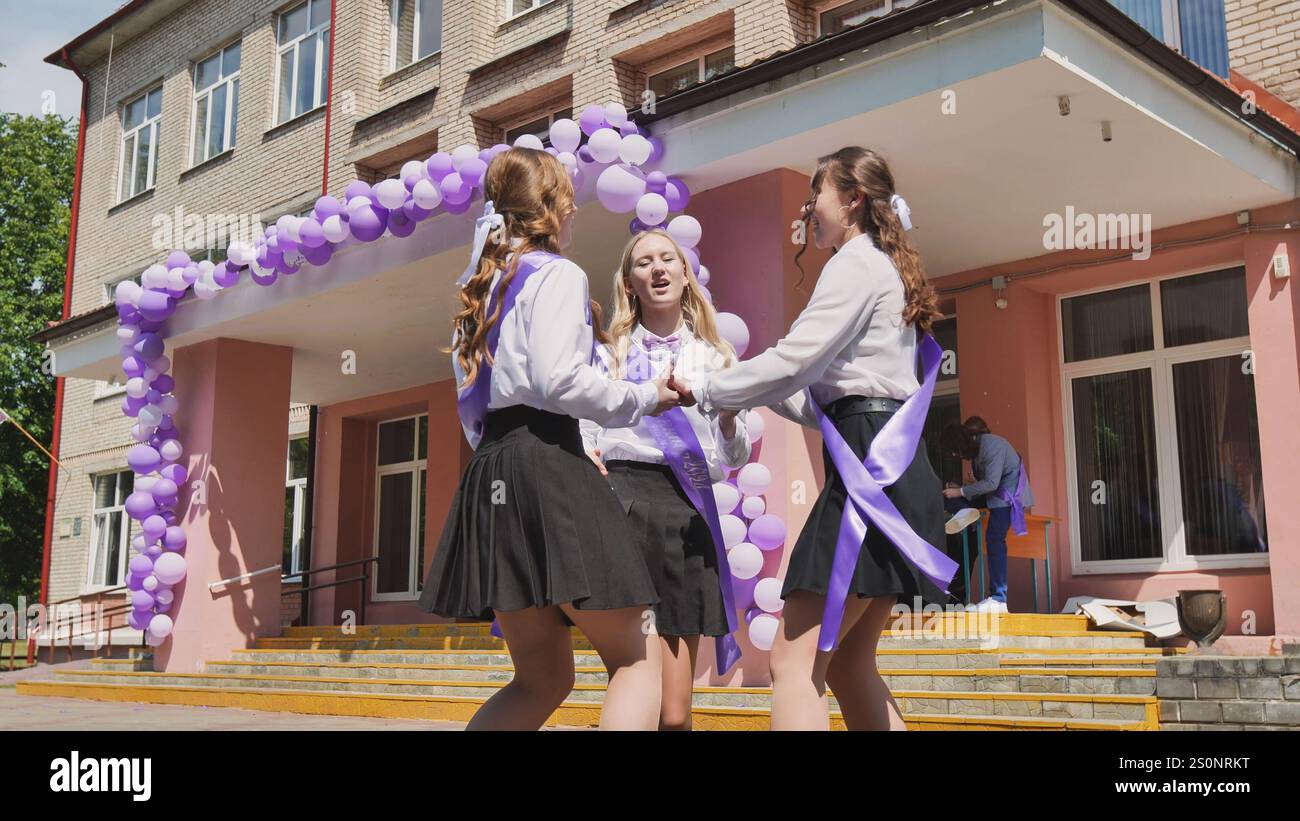 Three cheerful female students with purple ribbons are dancing and ...