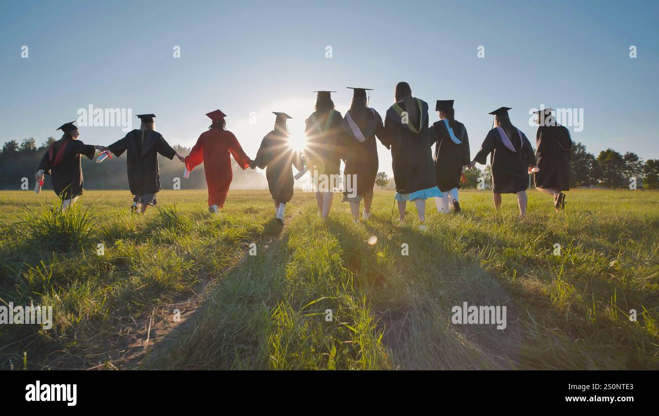 Students in graduation robes walking hand in hand through a sunset ...