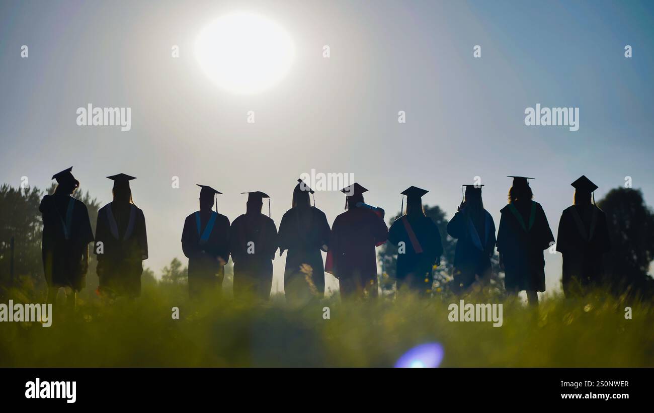 Graduates in cap and gown stand in a field at sunset, commemorating ...