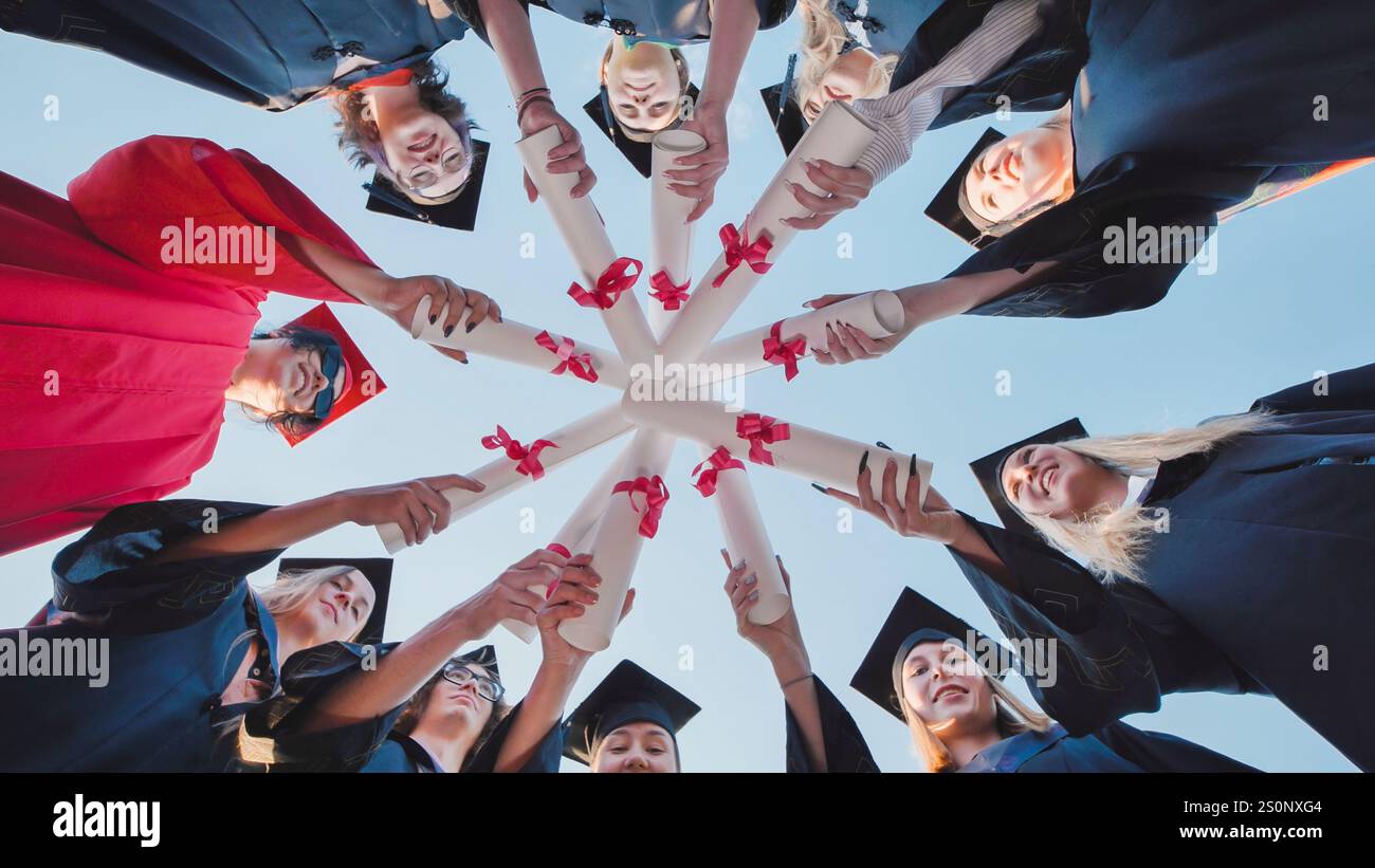 Joyful group of graduates in graduation attire forming a circle with ...