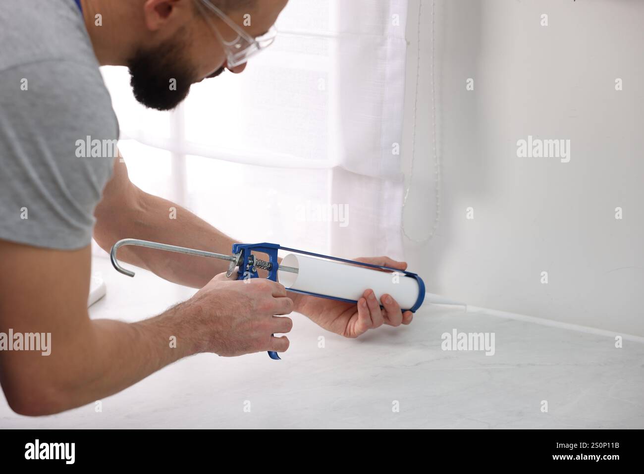 Man with caulking gun sealing countertop indoors Stock Photo - Alamy