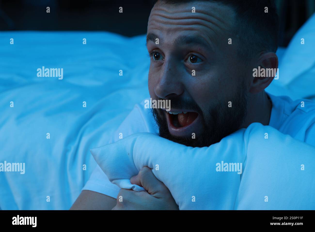 Fear of darkness. Scared man hugging pillow in bedroom at night Stock ...