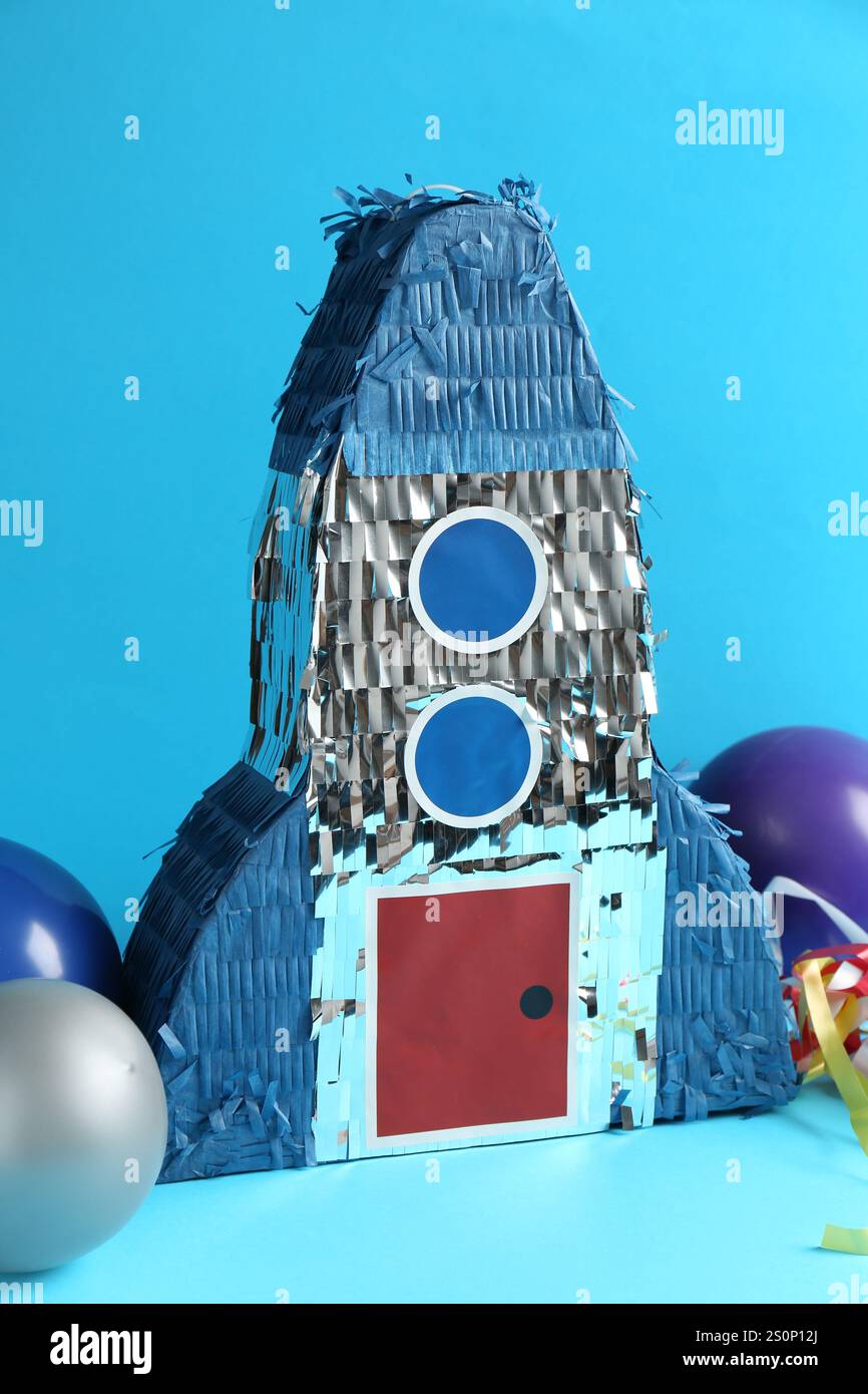 Beautiful pinata in shape of rocket and balloons on blue background ...