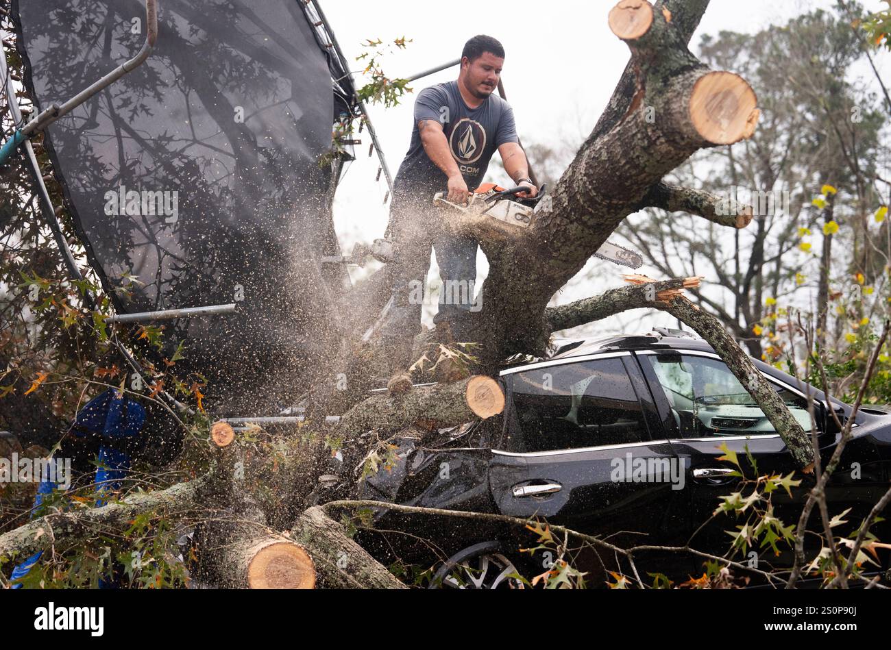 Saul Rodriguez uses a chain saw to remove debris atop a car from a ...