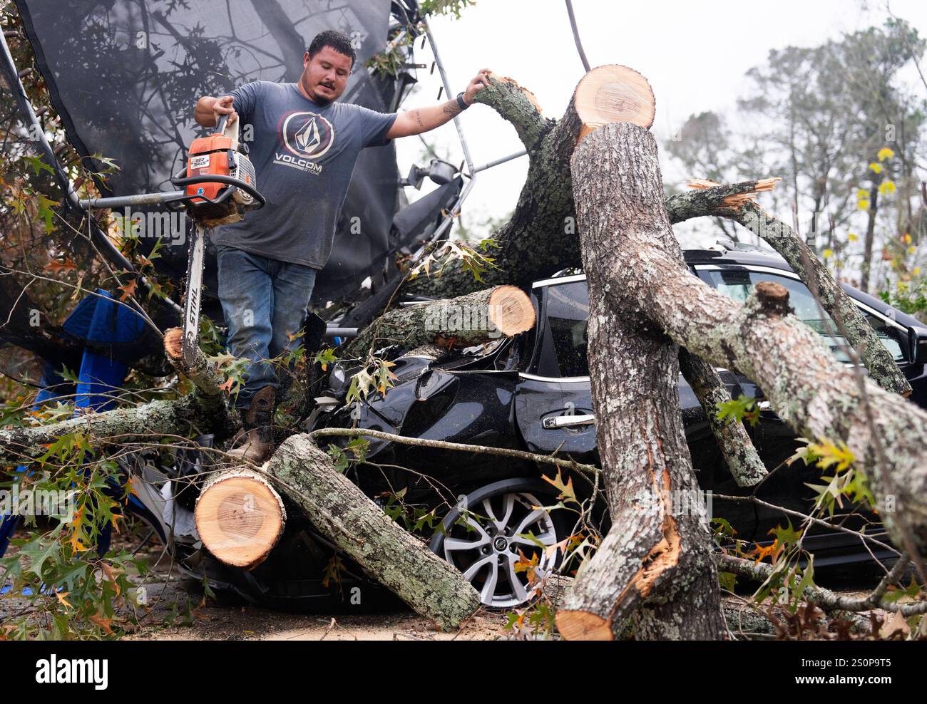 Saul Rodriguez uses a chain saw to remove debris atop a car from a ...