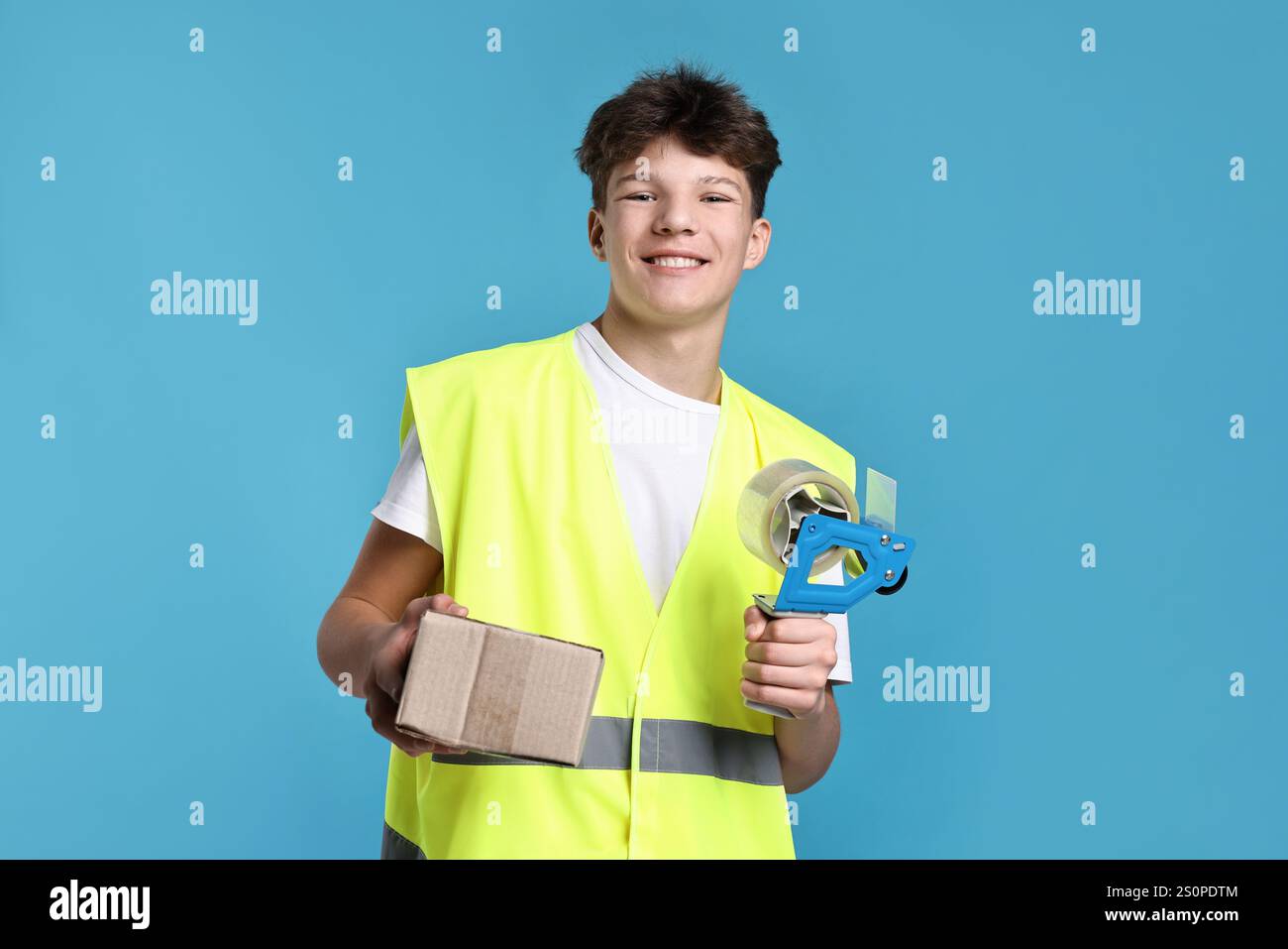 Teenage boy with tape gun dispenser and box in safety vest working as ...