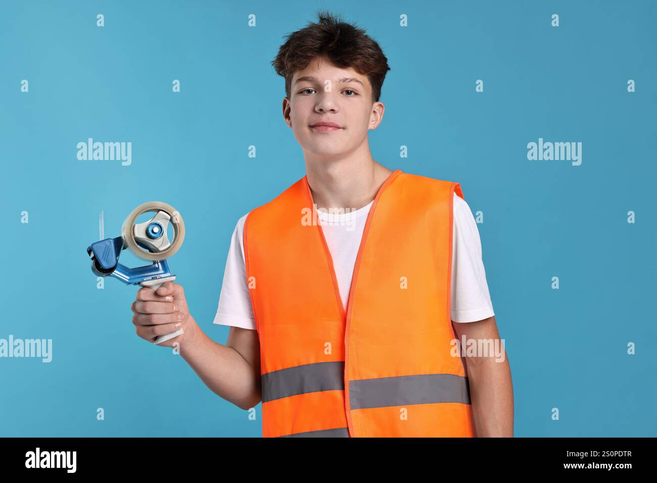 Teenage boy with tape gun dispenser in safety vest working as warehouse ...