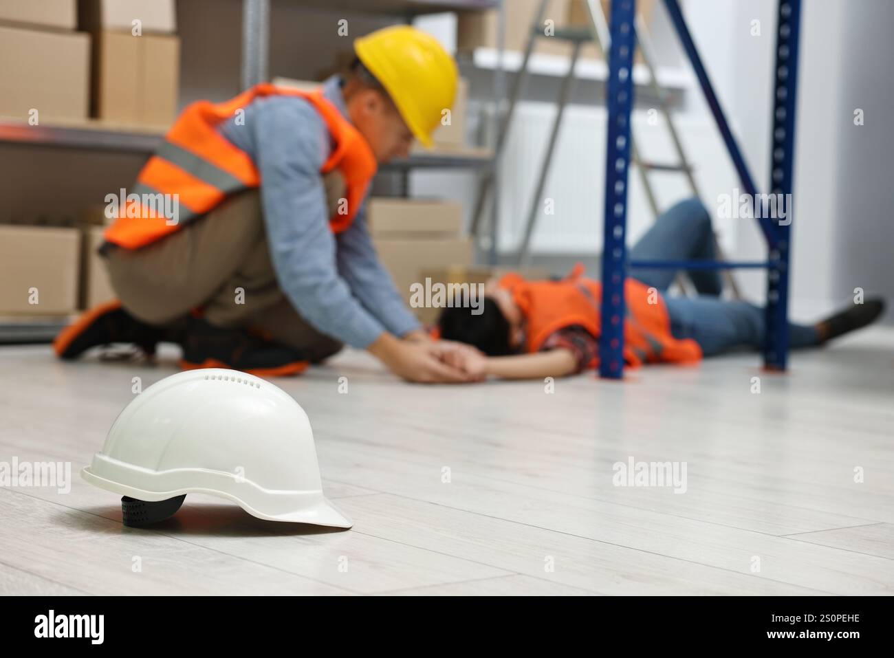 First aid. Hardhat on floor and man helping his unconscious colleague ...