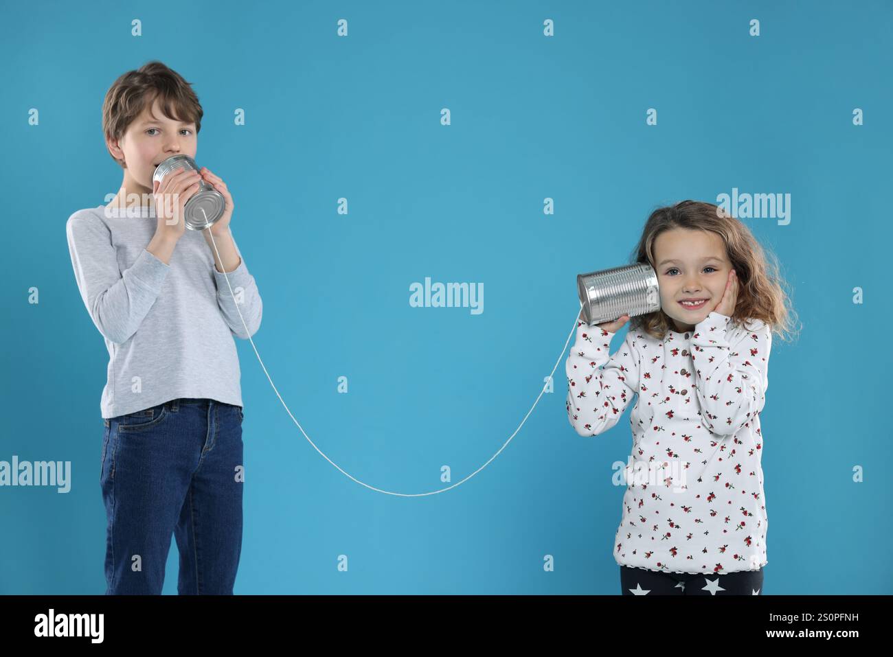 Boy and girl talking on tin can telephone against blue background Stock ...