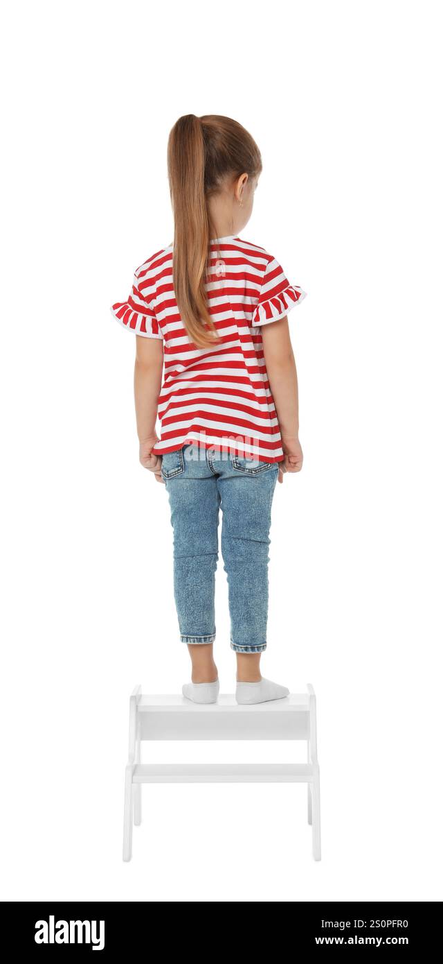 Little girl standing on step stool against white background, back view ...