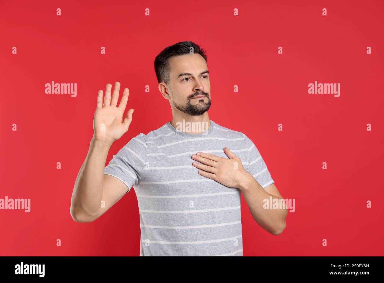 Man making promise with raised hand on red background. Oath gesture ...