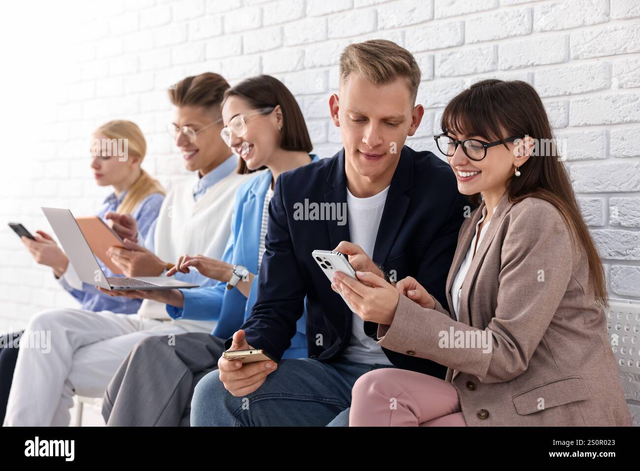 Group of people using different gadgets near white brick wall indoors ...