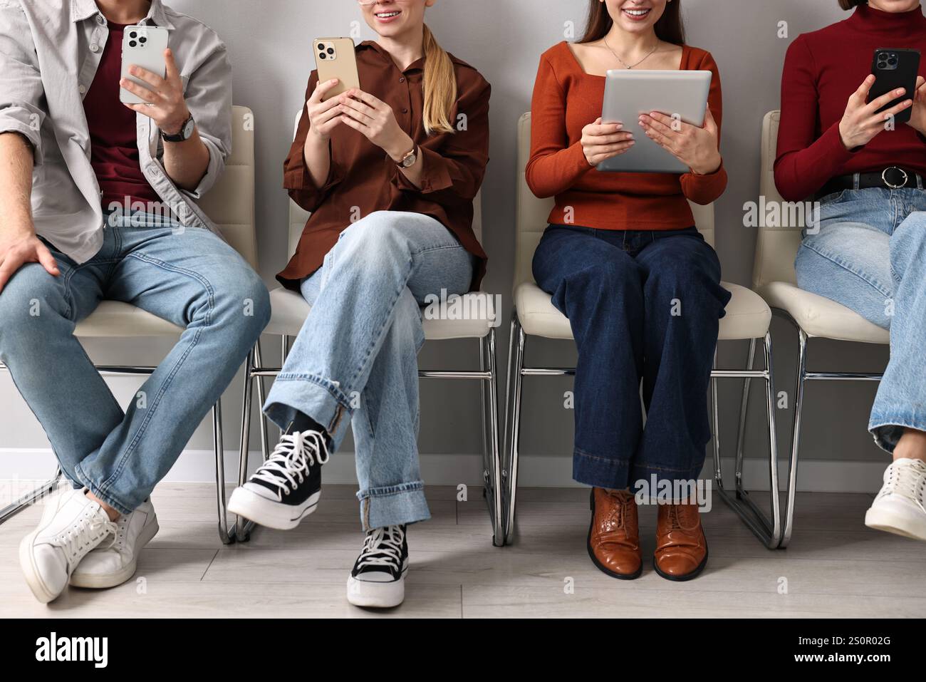 Group of people using different gadgets on chairs near grey wall ...