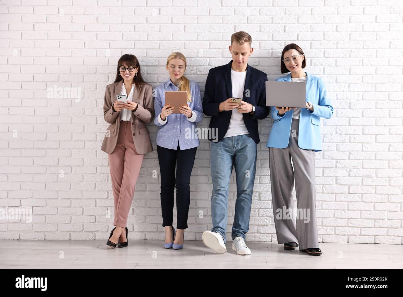 Group of people using different gadgets near white brick wall indoors ...