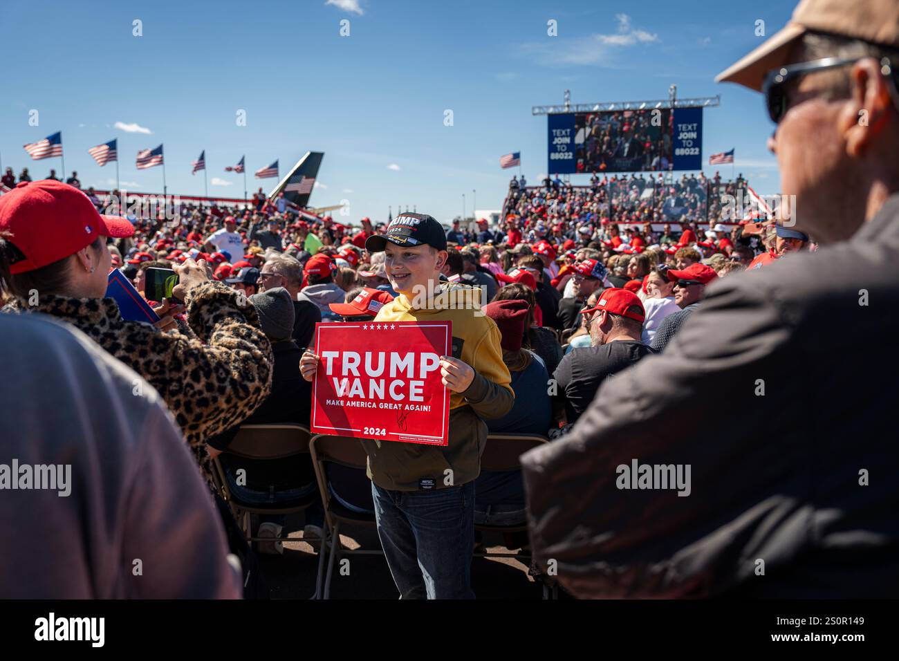 A young man poses for a photo holding a Trump Vance sign at an outdoor ...