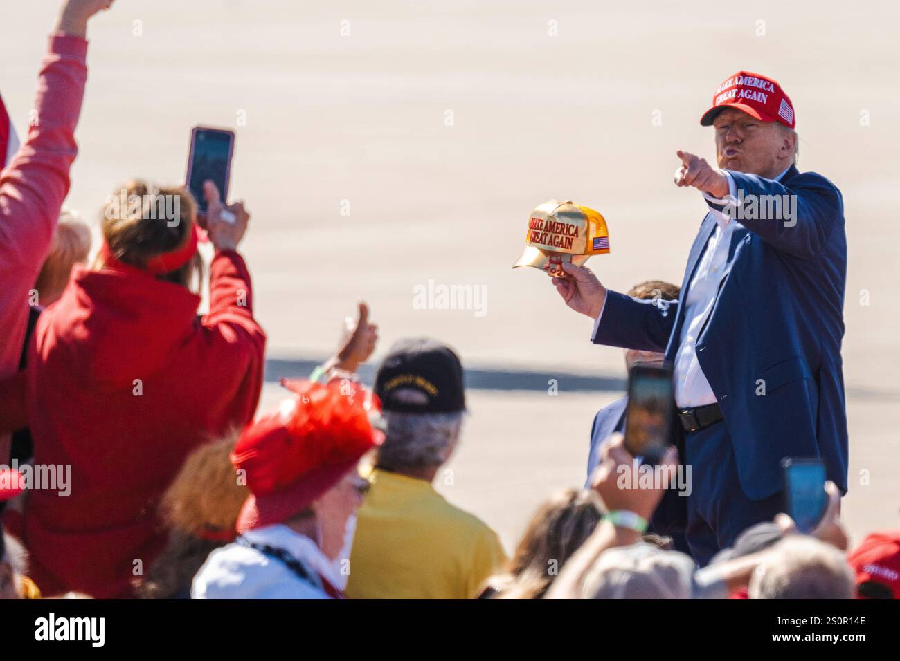 Donald Trump points at the crowd while holding a gold MAGA hat at rally ...