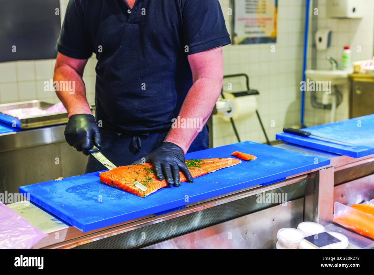 Fishmonger slicing fresh salmon fillet on blue cutting board at seafood ...