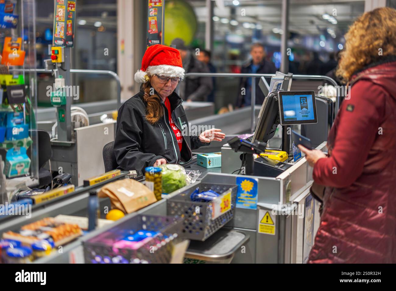 Cashier in Santa hat serving customer at grocery store checkout counter ...