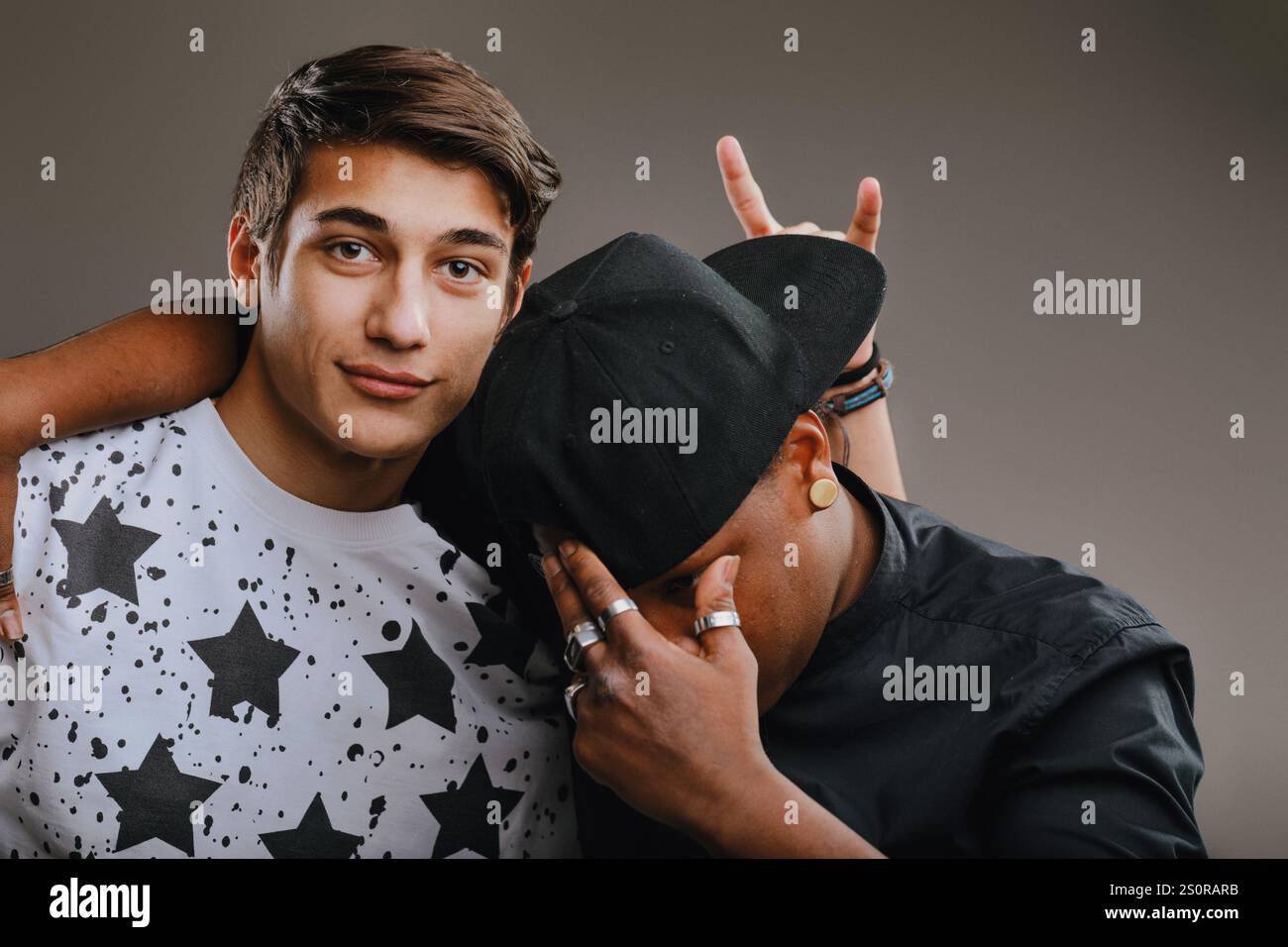 Two male friends smiling and making playful hand gestures, wearing ...