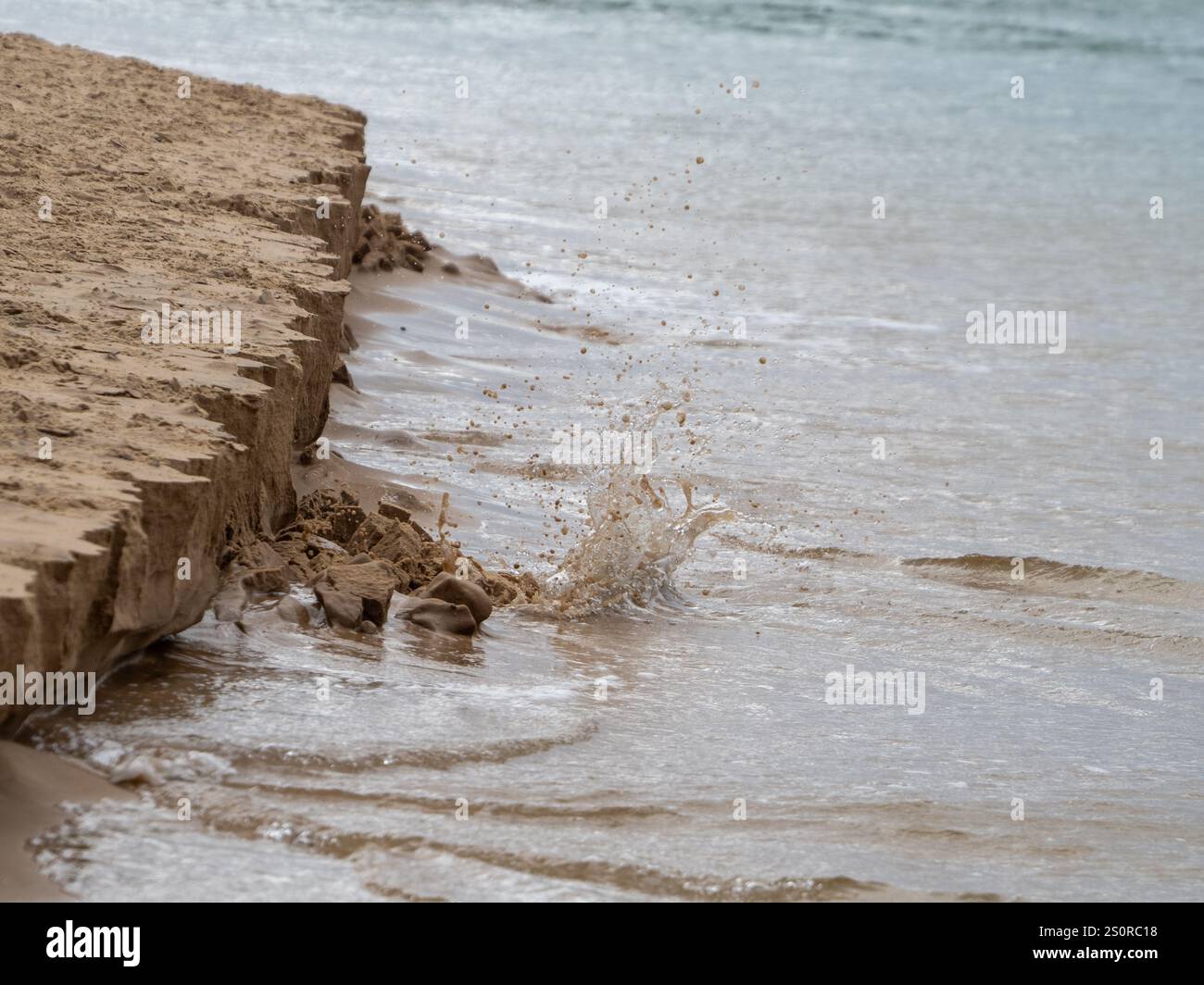 Sand and sea water splashing up into the air as the tide erodes it from ...