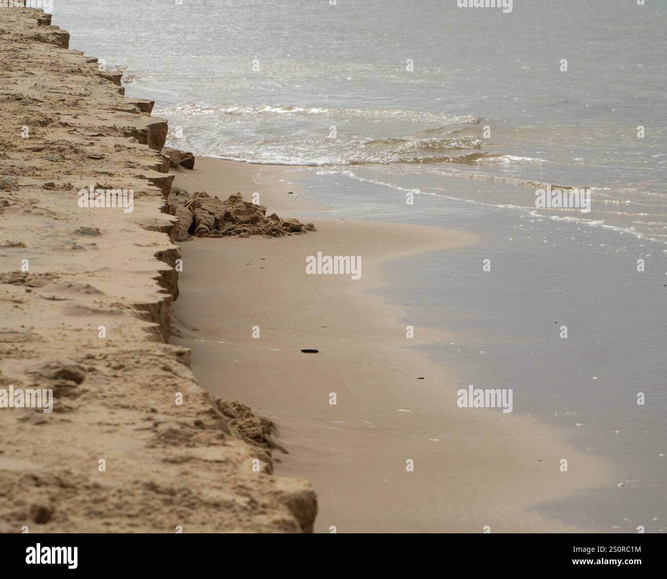 Sand eroding from beach edge, crumbling and falling down as tidal sea ...