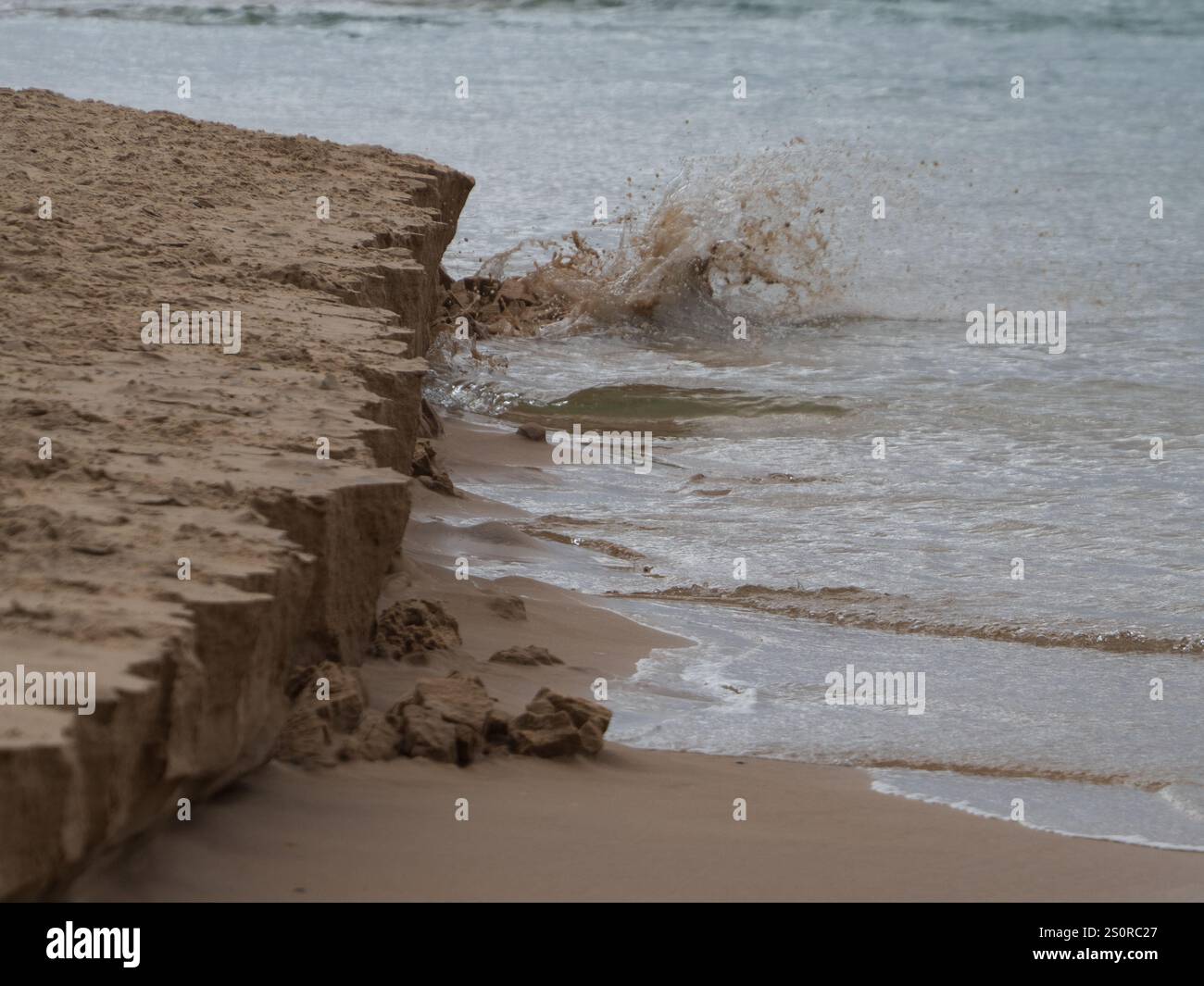 Sand and sea water splashing up into the air as the tide erodes it from ...
