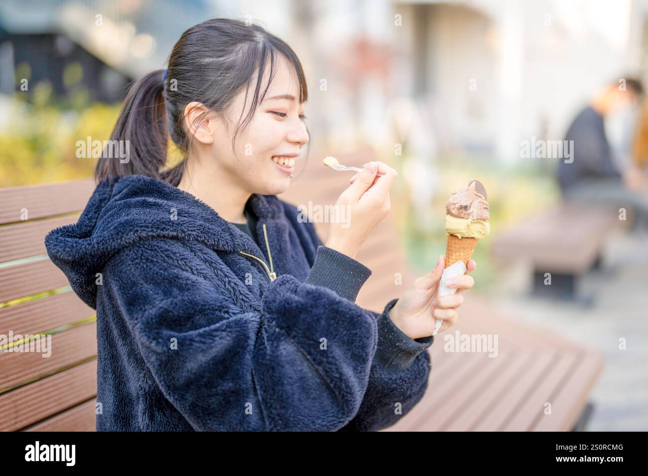 Cute woman in her early twenties eating gelato deliciously on bench in ...