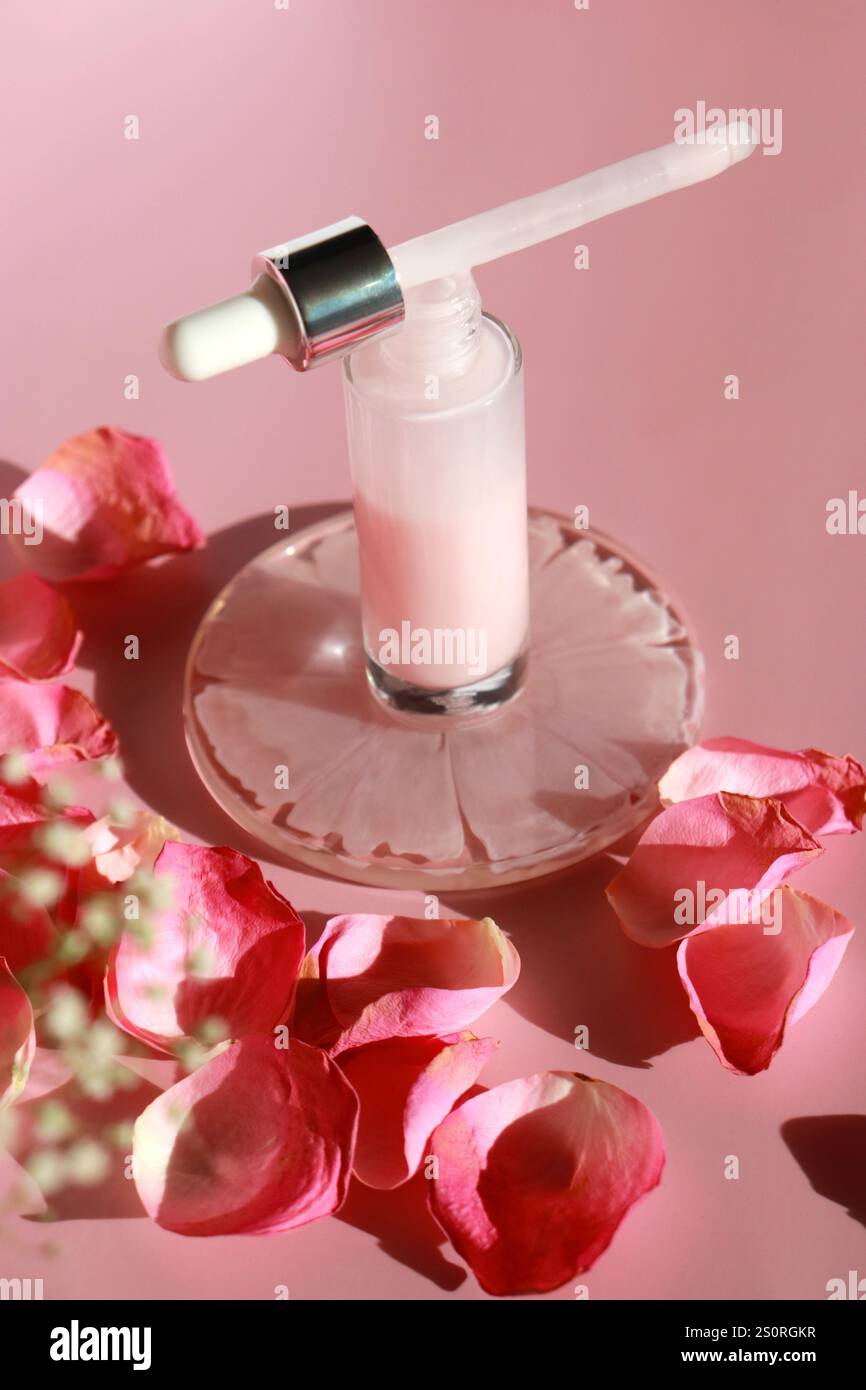 A bottle of facial serum lotion with roses extract on pink background ...