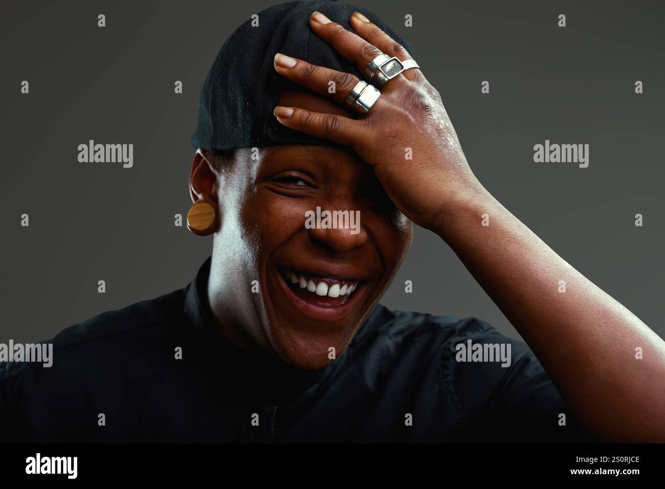 Studio portrait of a cheerful young adult wearing a baseball cap, rings ...