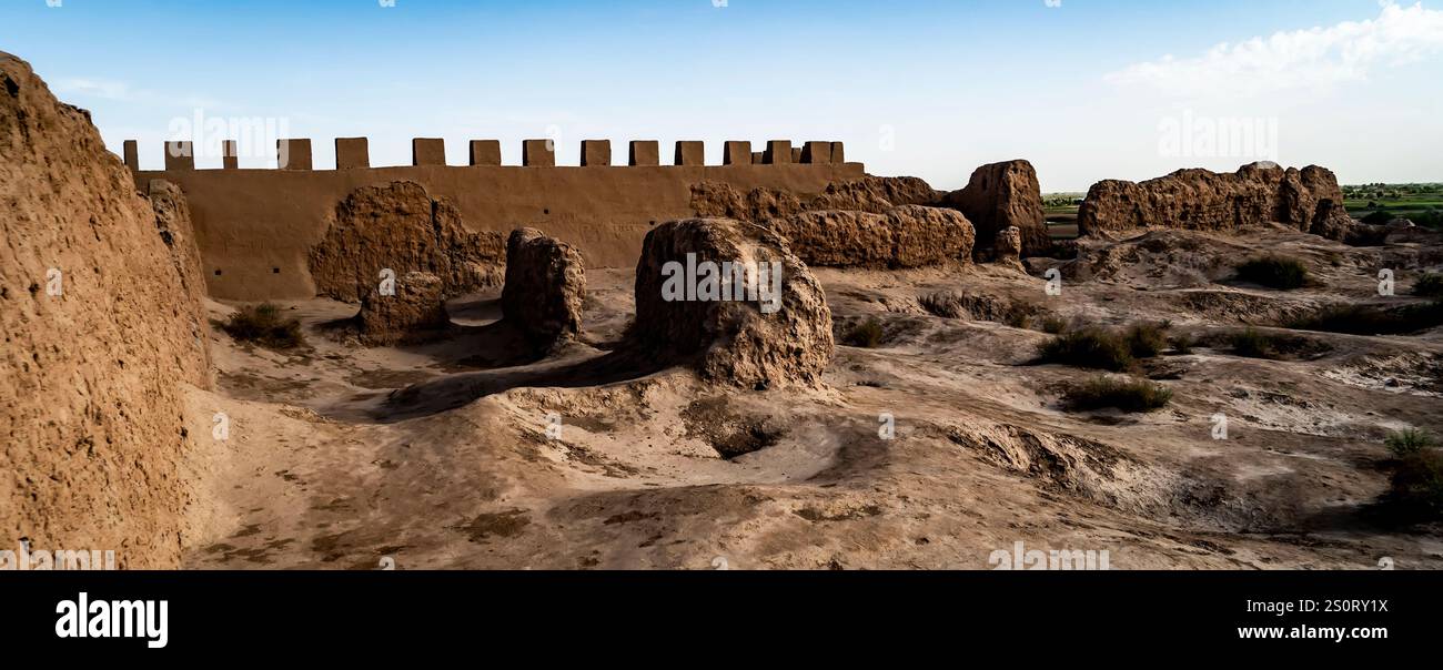 A panoramic view of ancient ruins with a mud-brick wall in the background. The landscape ...