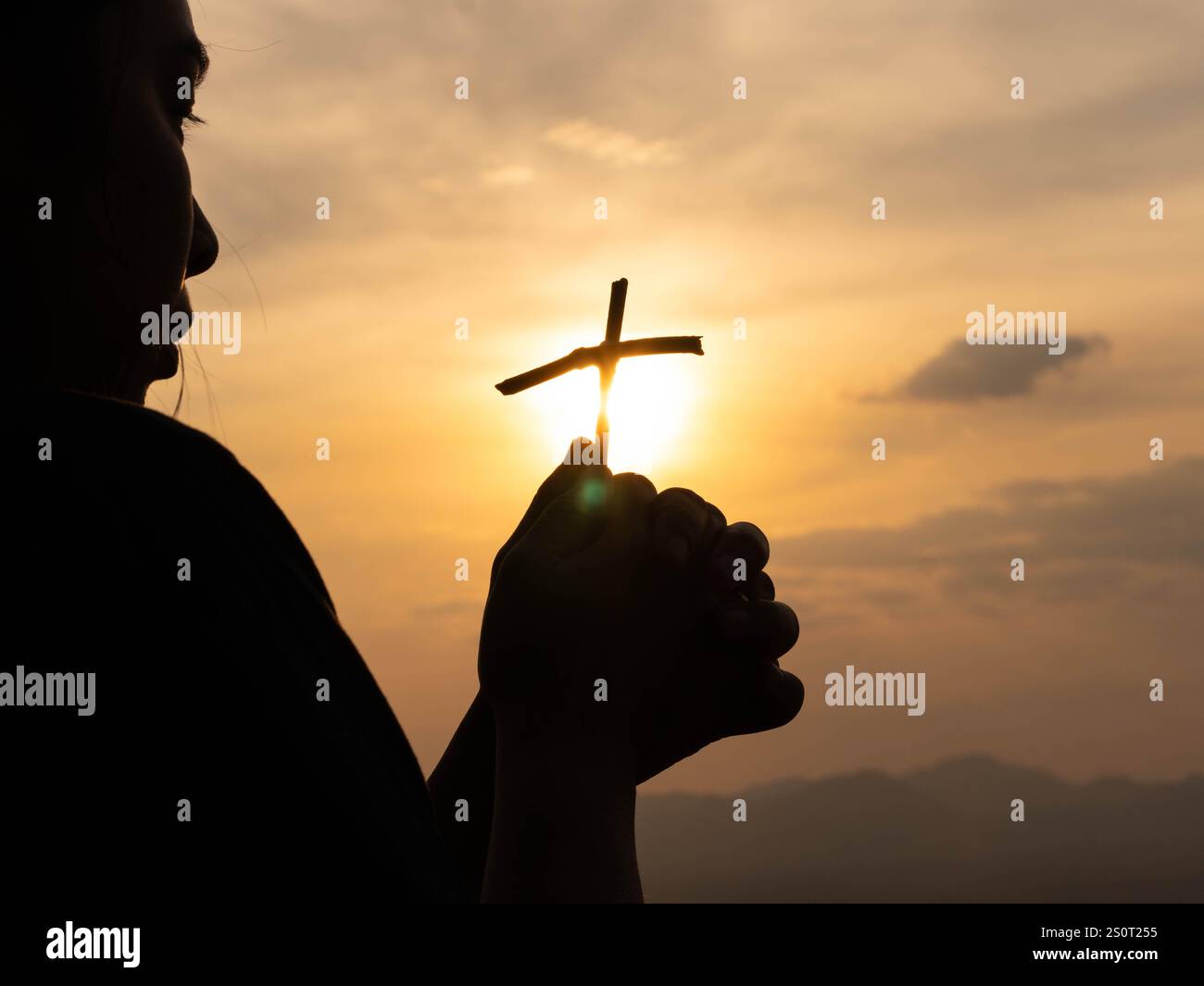 Silhouette of a Christian woman holding a cross praying at sunset ...