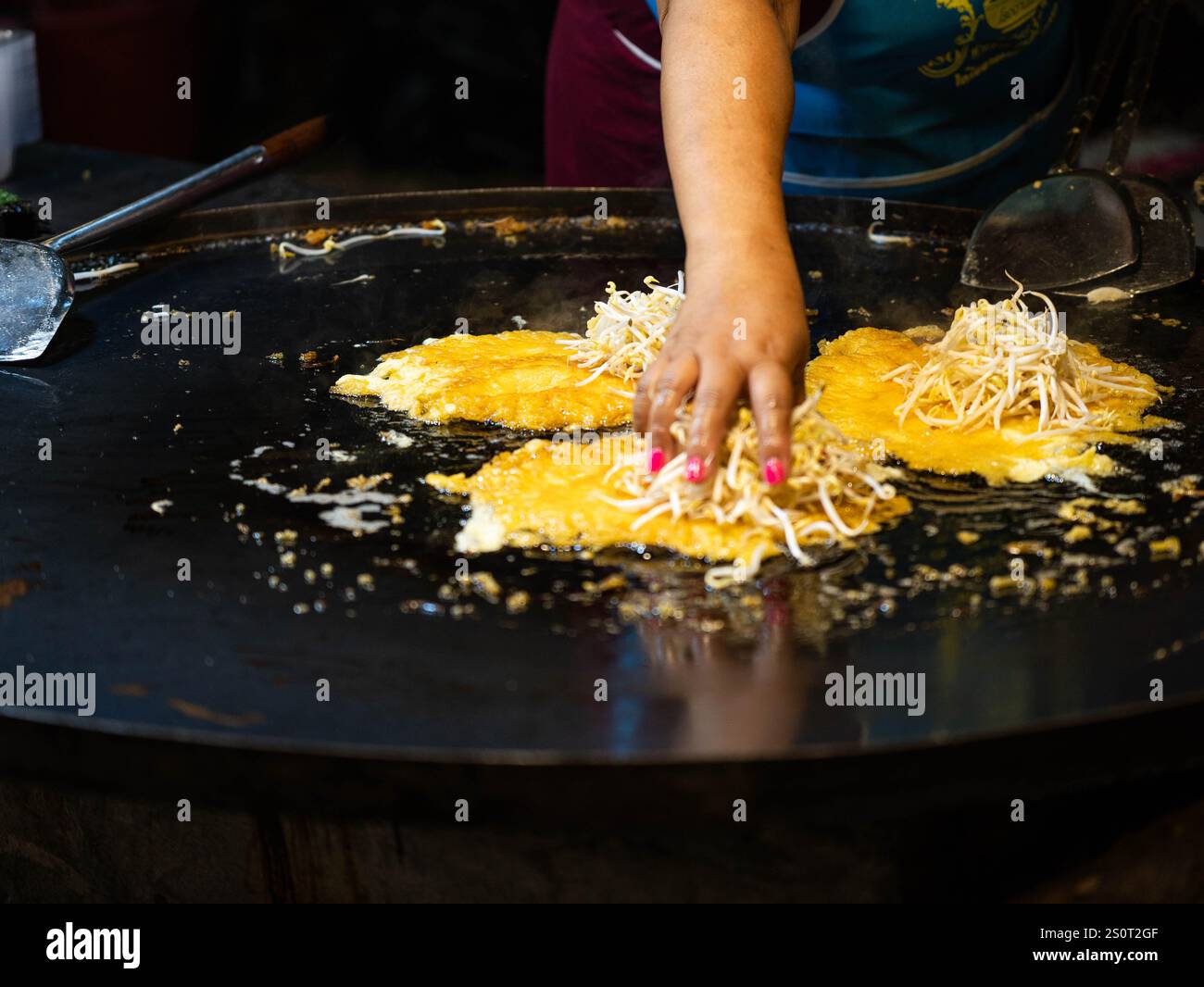 A person is cooking fried oysters in a circular pan. Street food in the ...