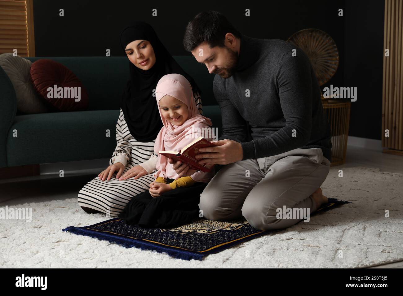 Muslim family with Quran praying on mat at home Stock Photo - Alamy