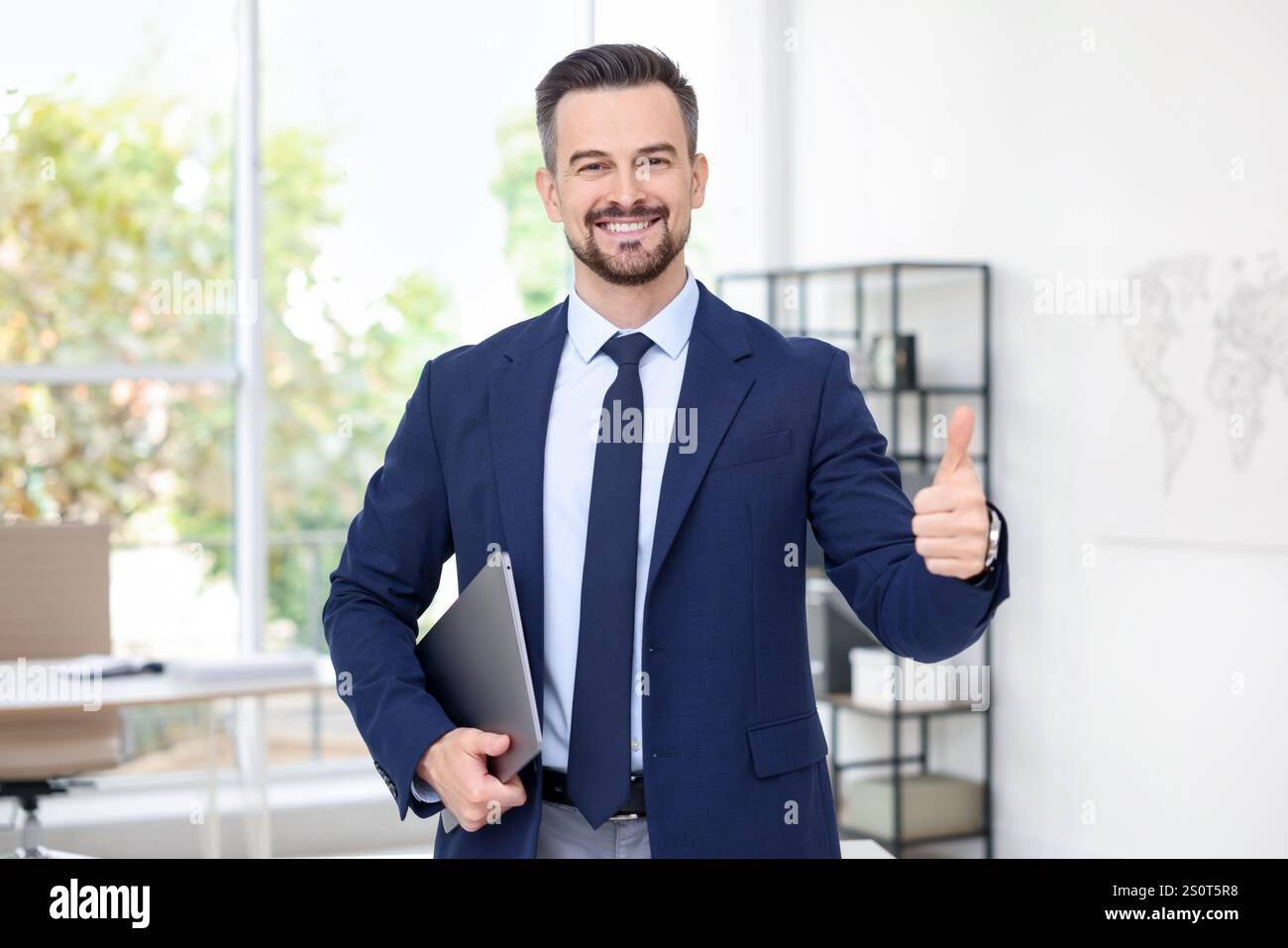 Portrait of smiling banker with laptop showing thumbs up in office ...