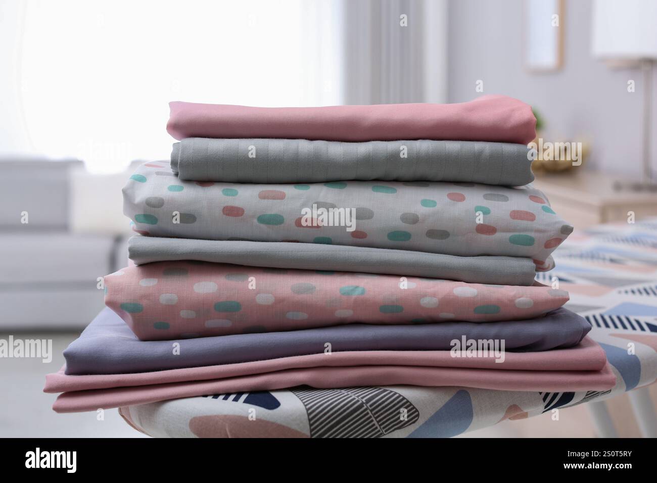 Stack of clean bed linens on ironing board in room Stock Photo - Alamy