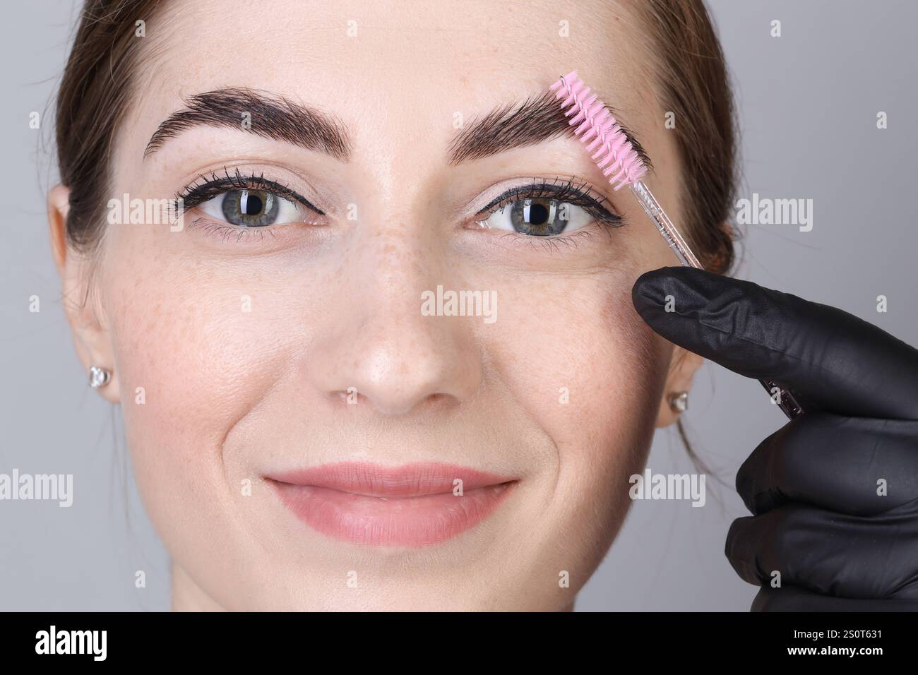 Brow lamination. Cosmetologist combing woman's eyebrows with brush ...