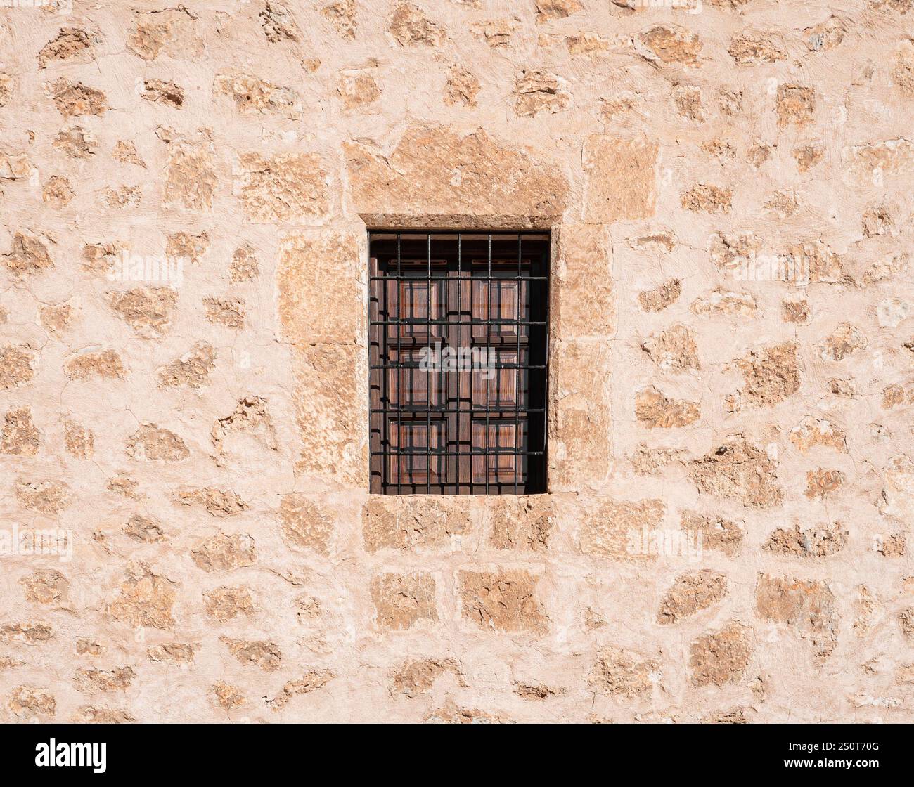Ancient Spanish stone wall with a metal iron grid window as a prison in ...