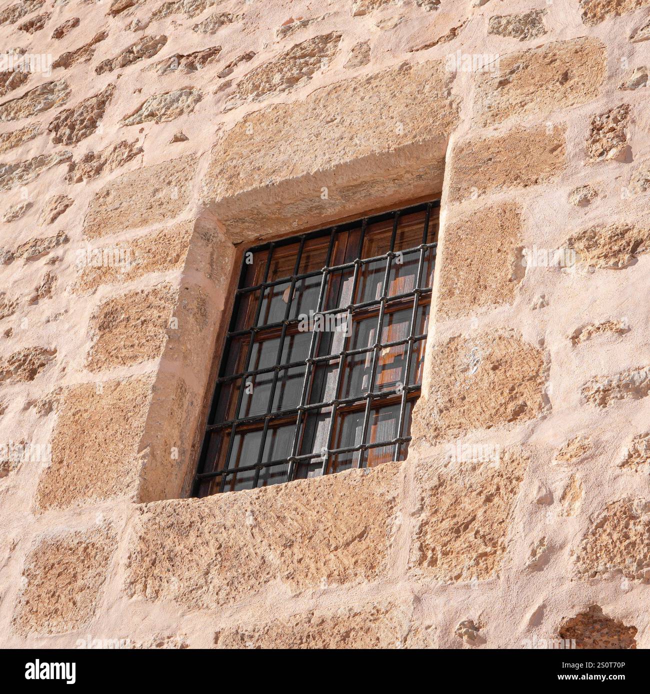 Ancient Spanish stone wall with a metal iron grid window as a prison in ...