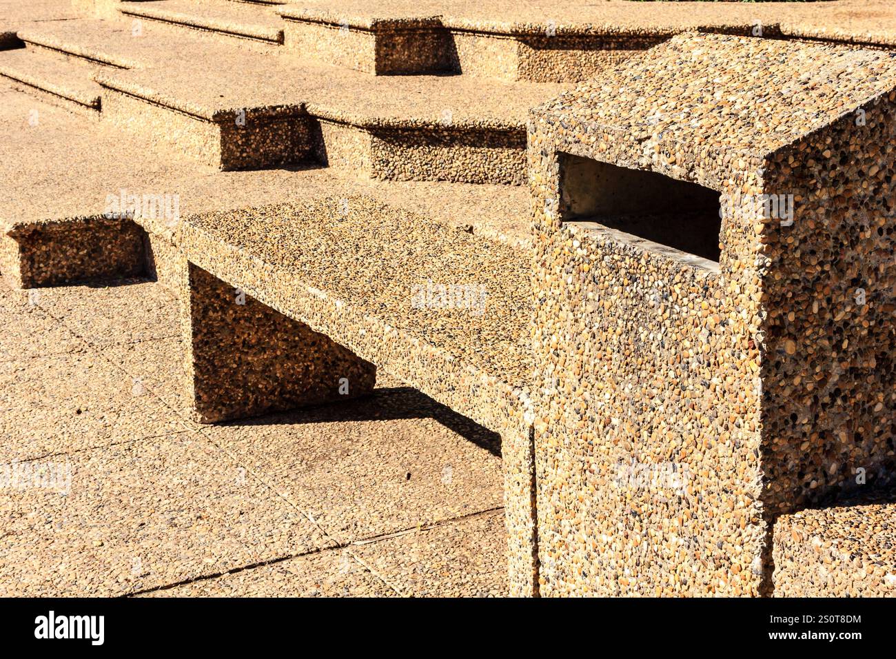 A bench is sitting on a concrete slab with a trash can nearby. The ...
