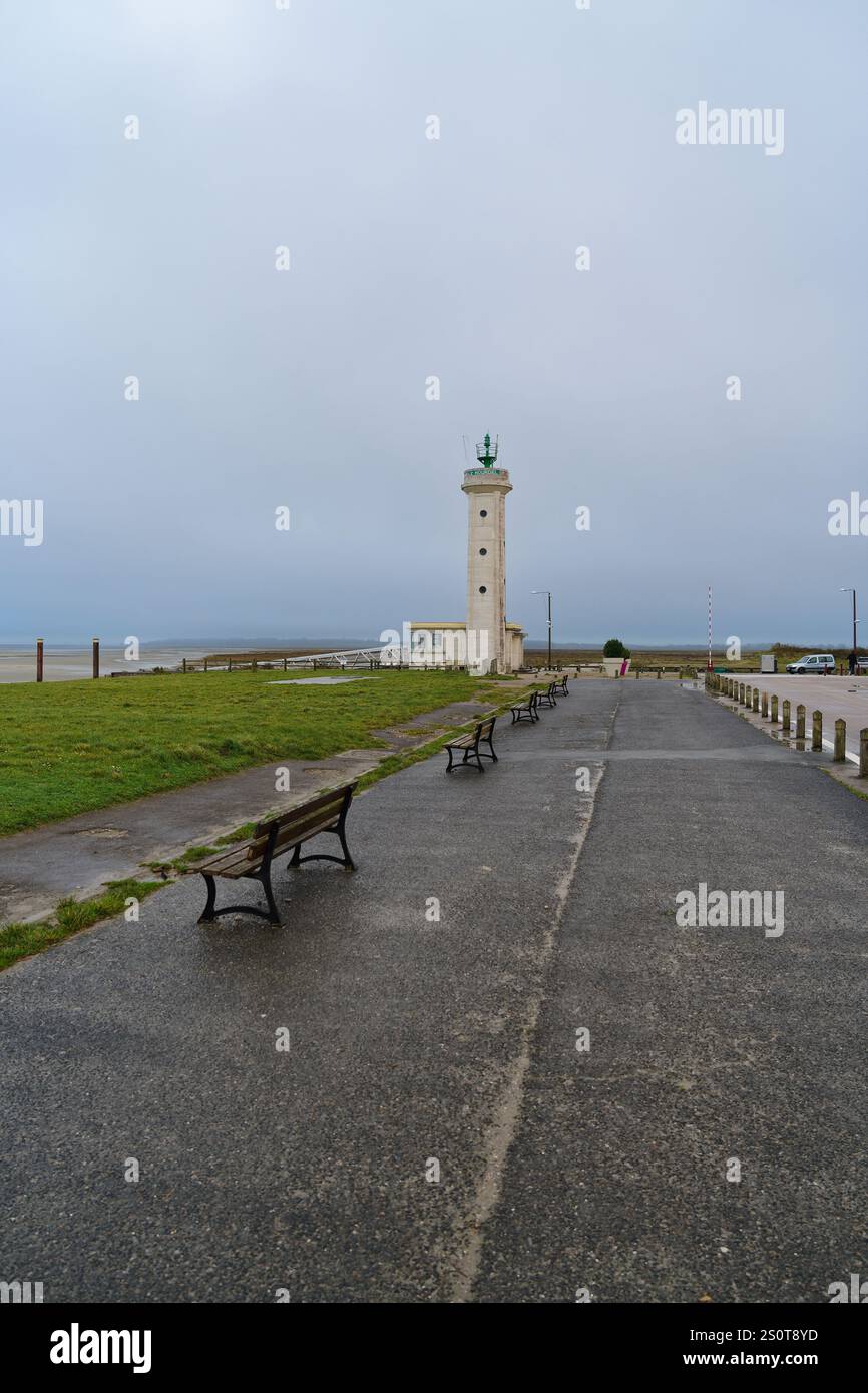 Coastal walkway with benches leading to a lighthouse on a cloudy day ...