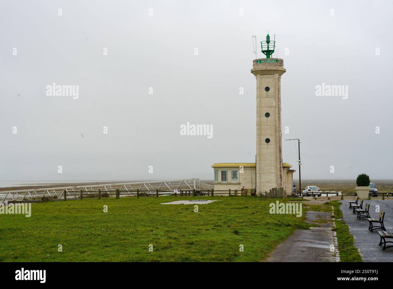 Coastal lighthouse stands tall on a foggy day by the shore with benches ...