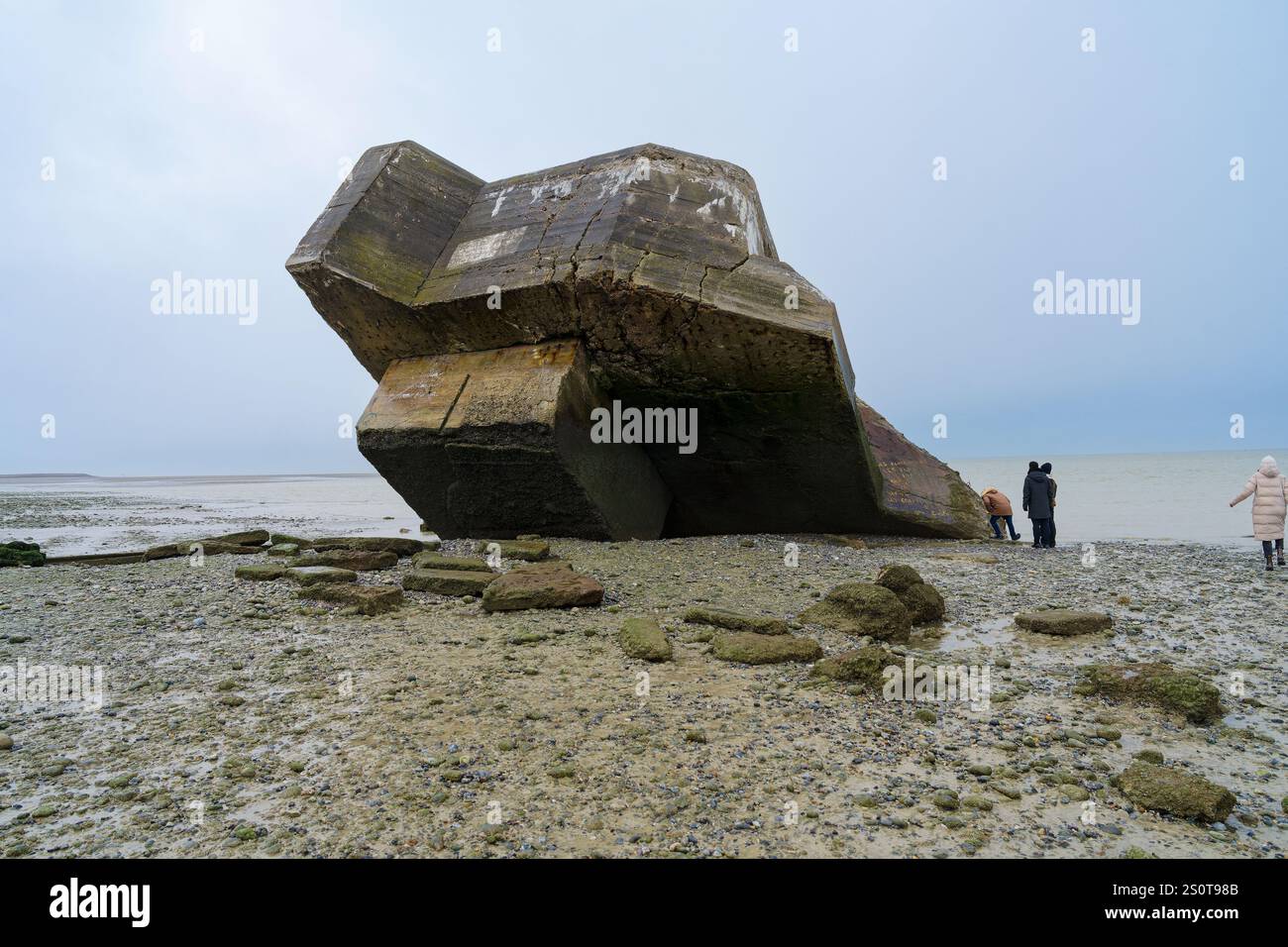 Concrete structure tilted on a sandy beach as visitors explore its ...