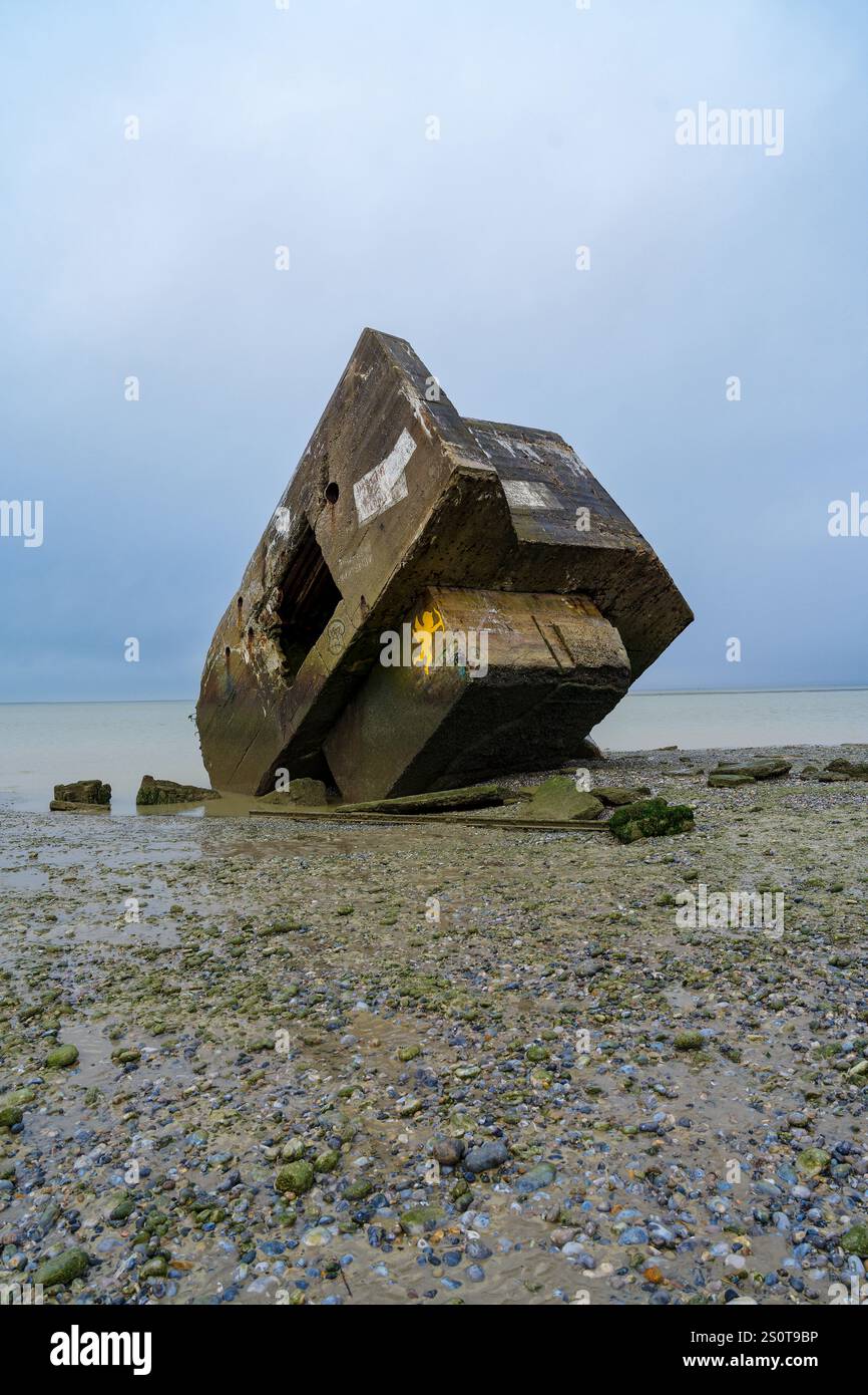 Ruined concrete structure partially submerged on a beach shore under a ...