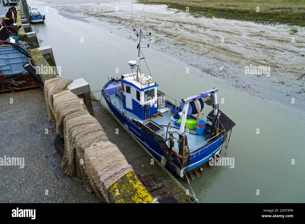 Fishing boat moored by the shoreline during low tide in a coastal area ...