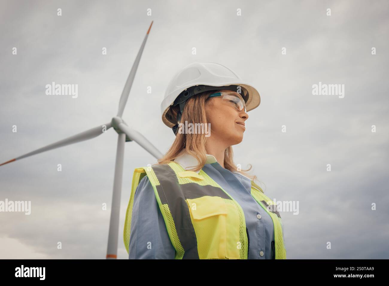 A Female Engineer stands confidently at a vast, sprawling wind farm ...