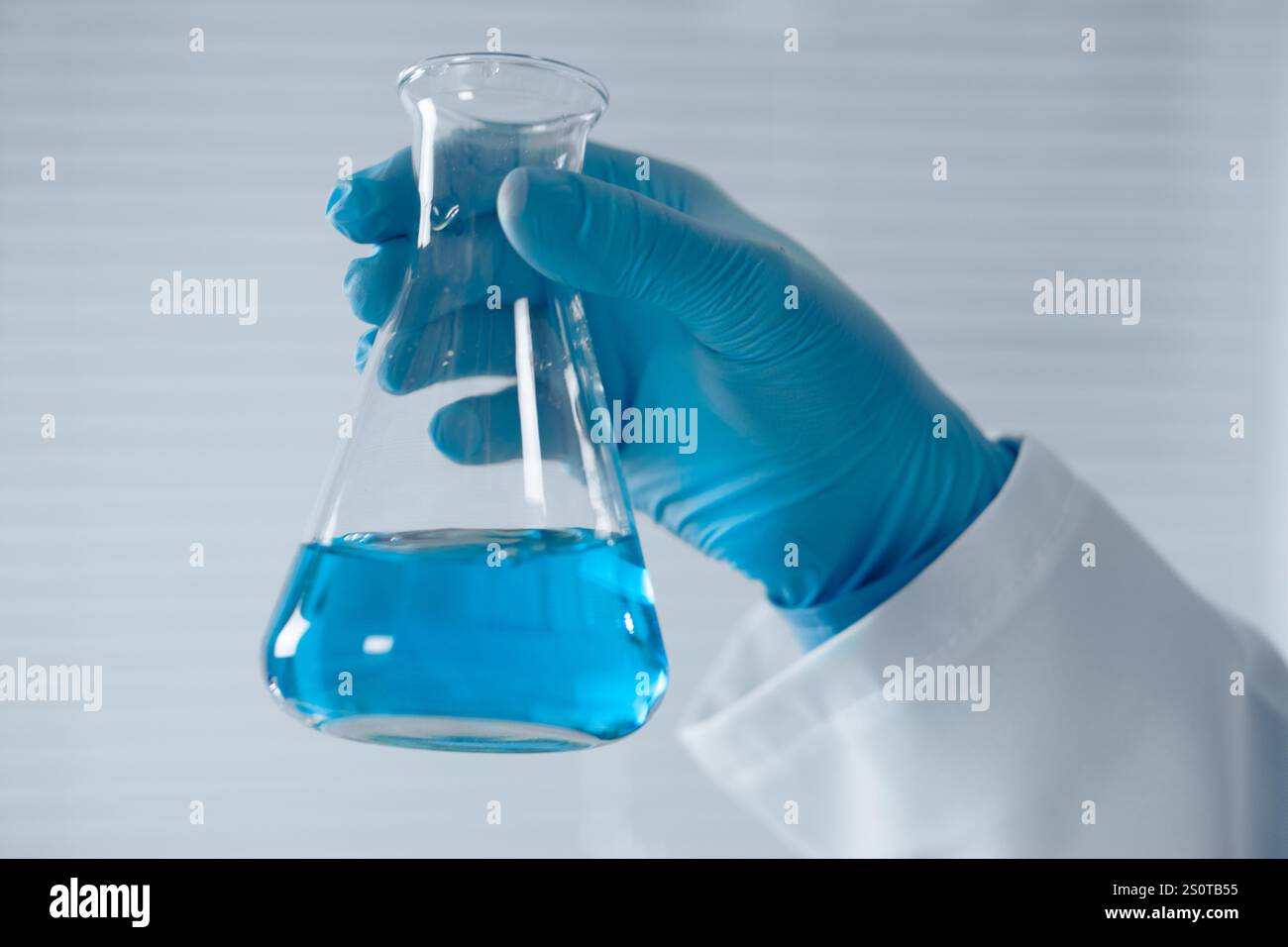 A dedicated scientist holds an Erlenmeyer flask with vibrant blue ...