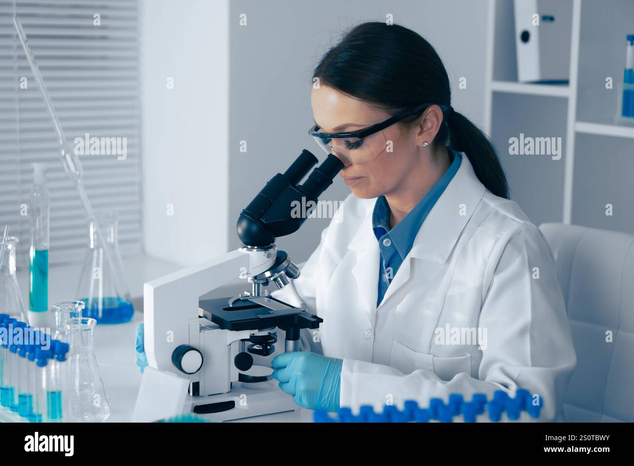 In a modern lab, a skilled female scientist analyzes biological and chemical samples under a ...