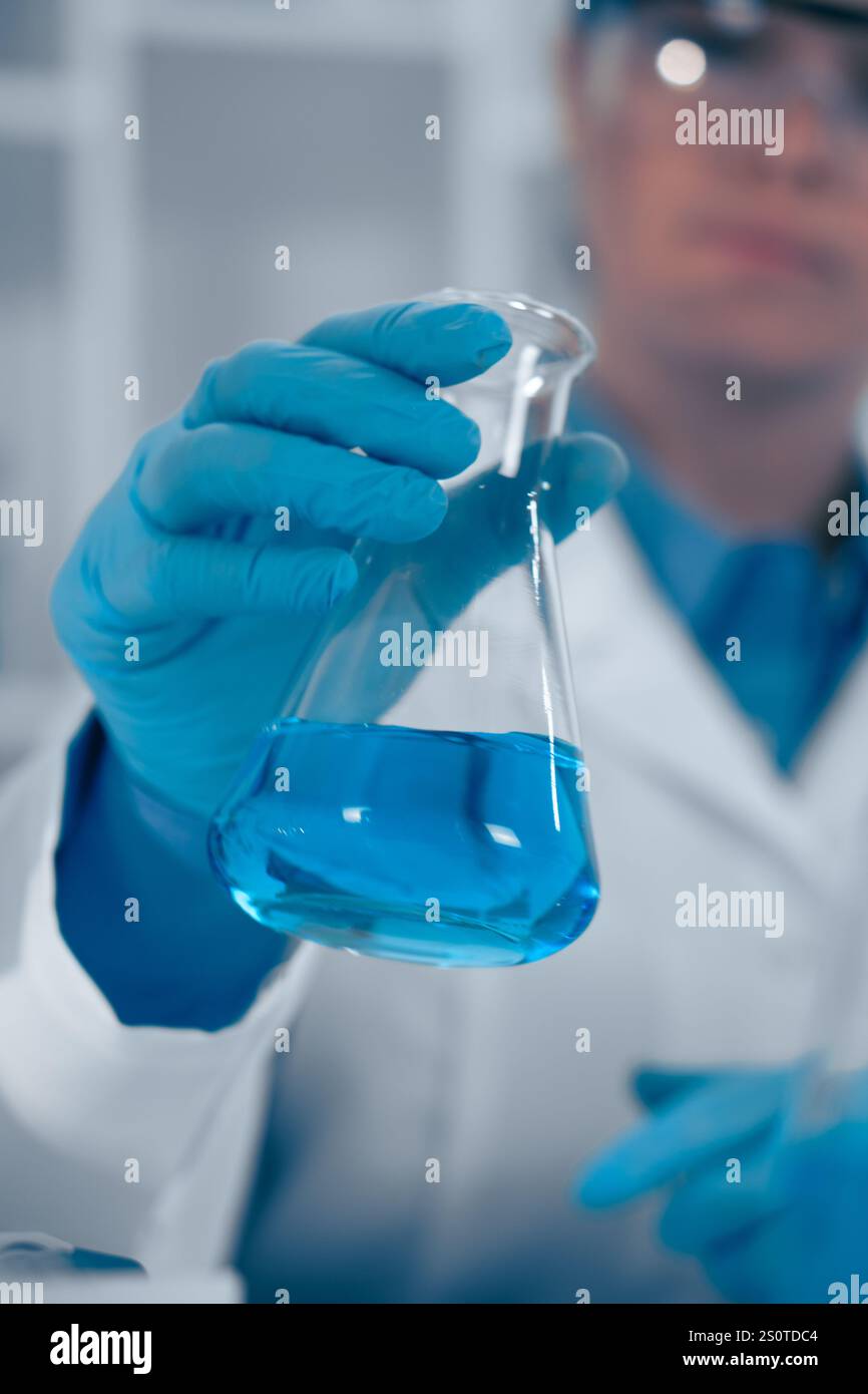 A scientist in a laboratory is holding a flask that contains a blue ...