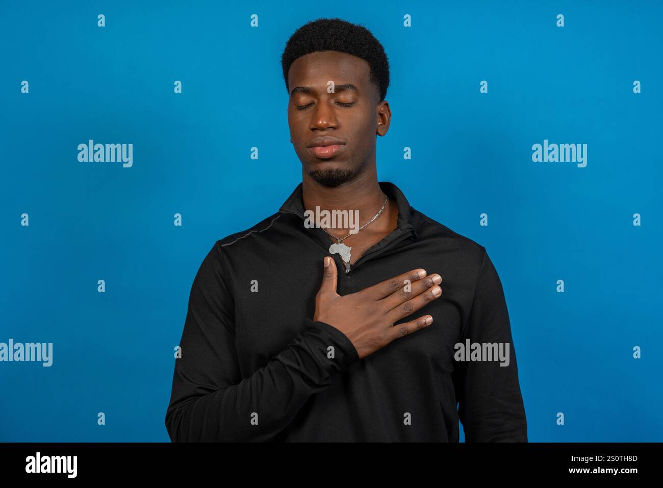 Studio portrait of a young black man with an africa pendant, hand on ...